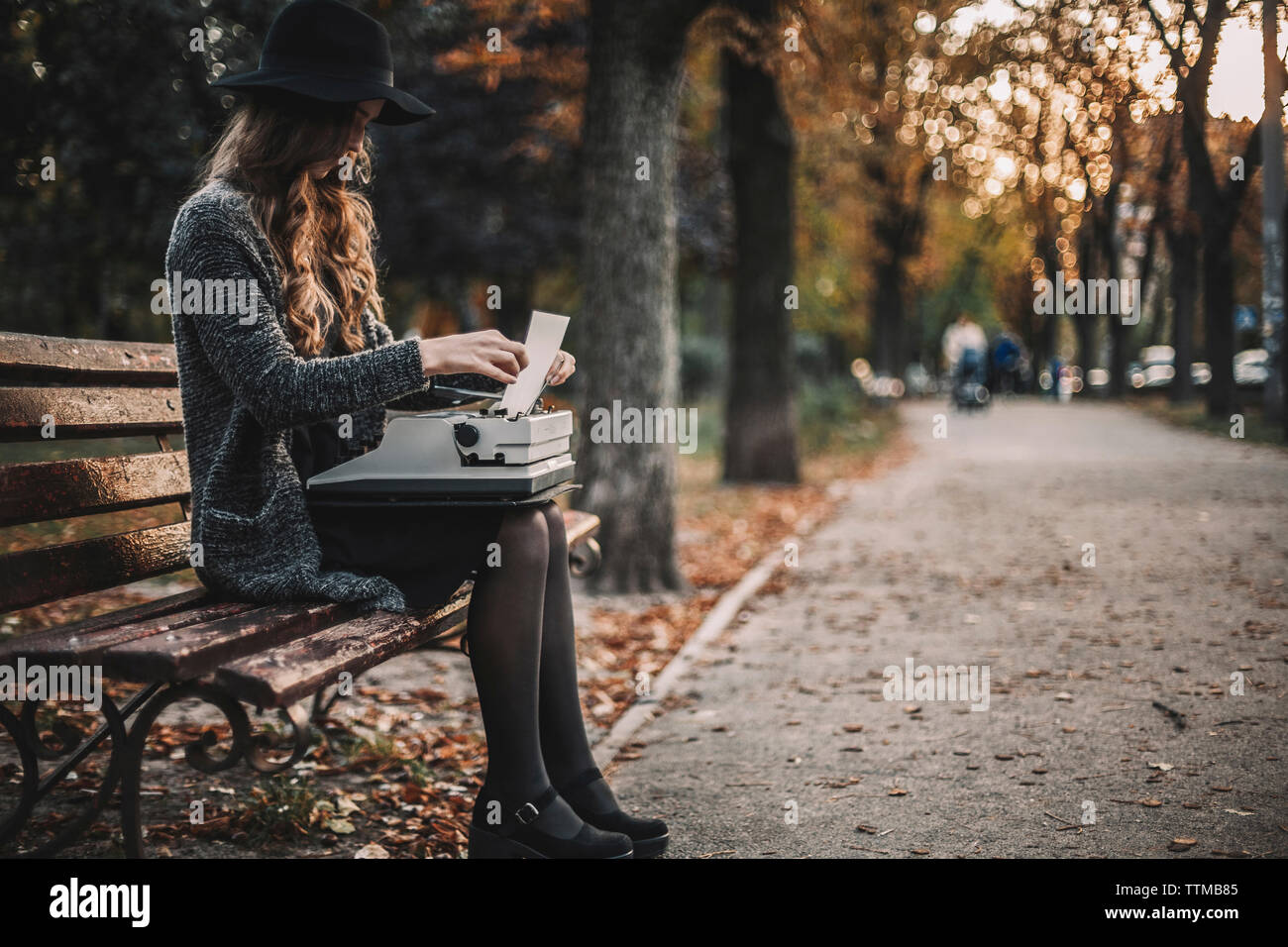 Side view of female writer using typewriter while sitting on bench at ...
