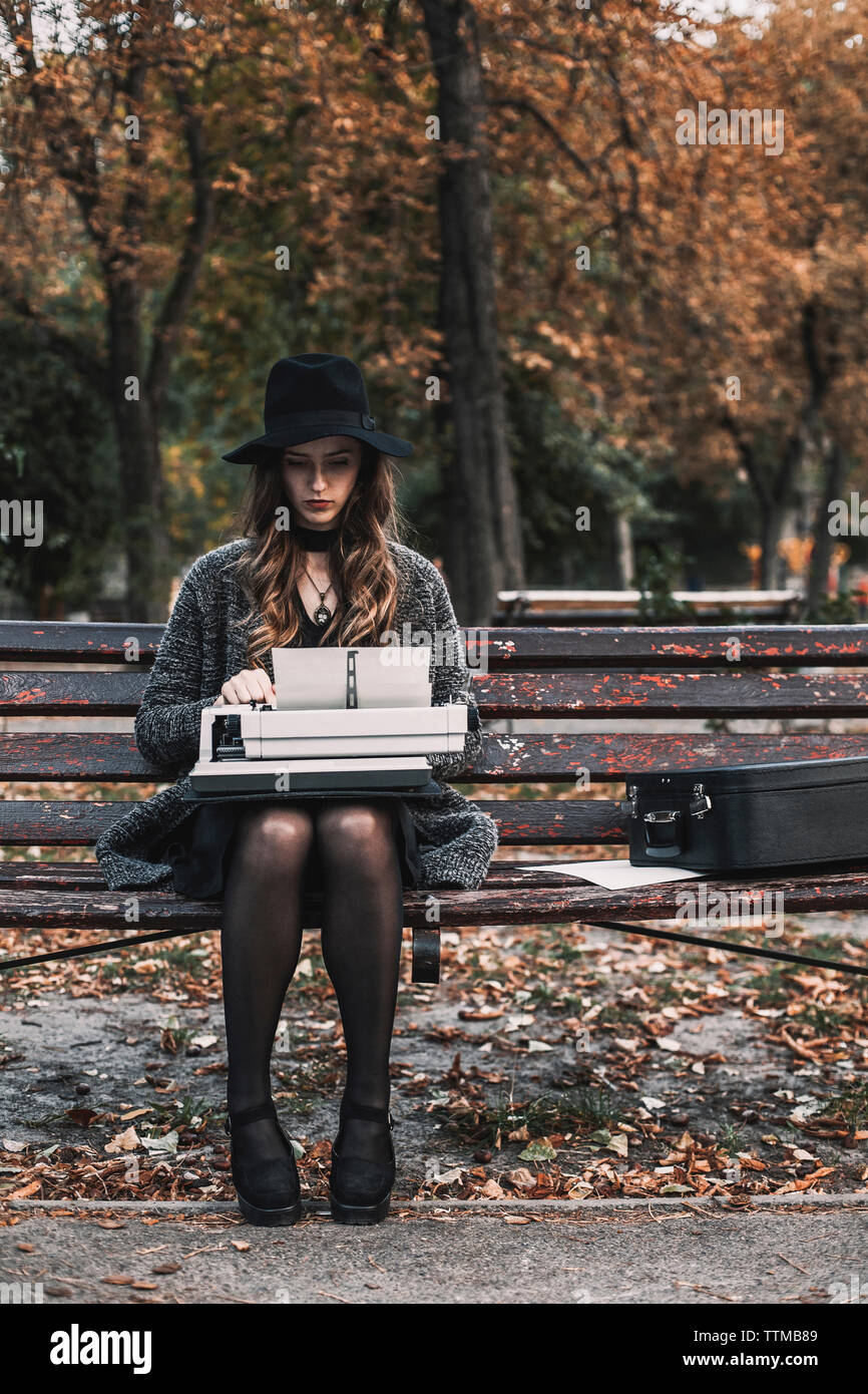 Female writer using typewriter while sitting on bench at park during ...