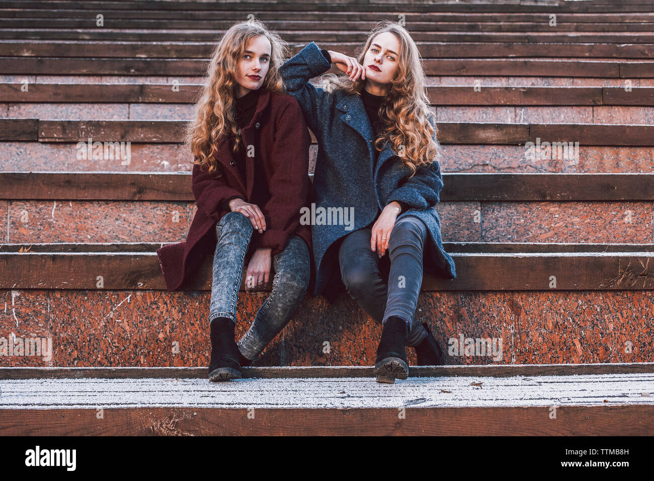 Portrait of sisters sitting on steps in city during winter Stock Photo ...