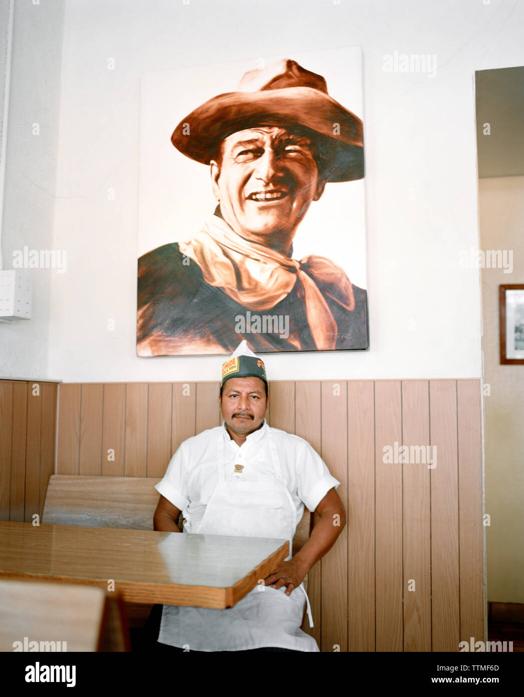 USA, New Mexico, cook sitting under John Wayne painting, Frontier ...
