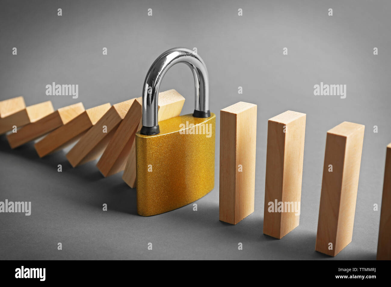 Lock blocked row of falling dominoes on grey background Stock Photo - Alamy