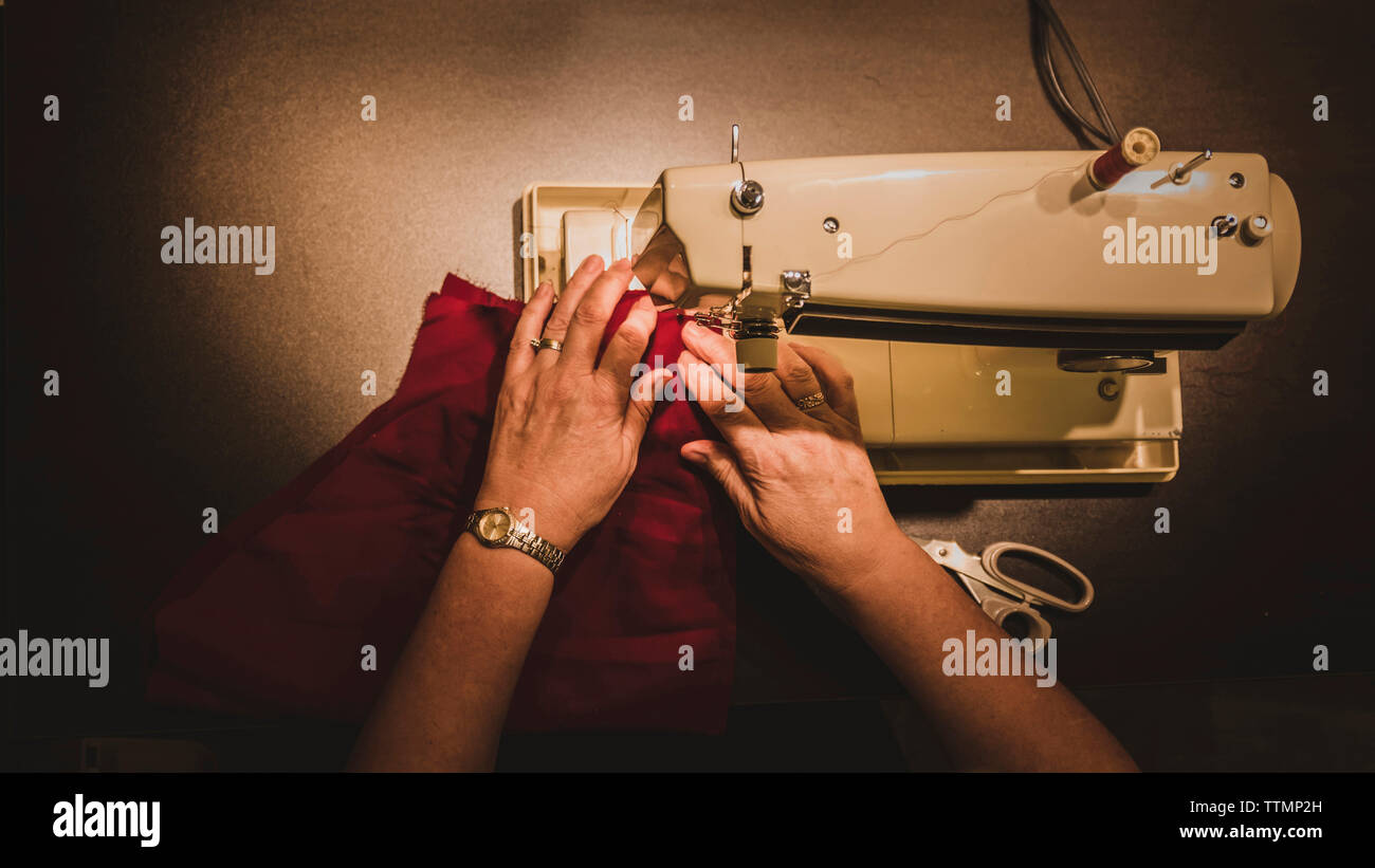 High angle cropped hands of woman using sewing machine at workshop ...