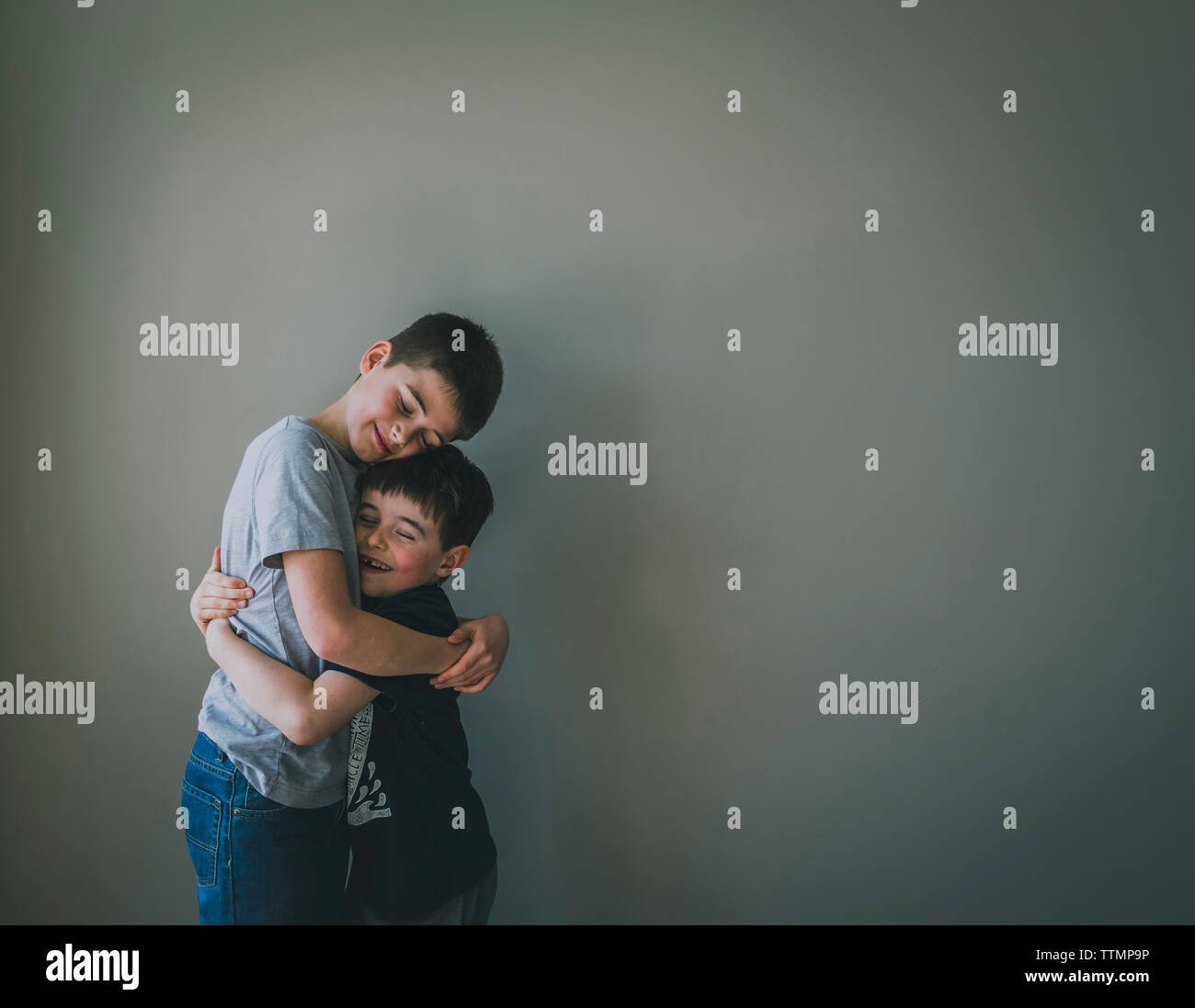 Smiling brothers embracing while standing by wall at home Stock Photo ...