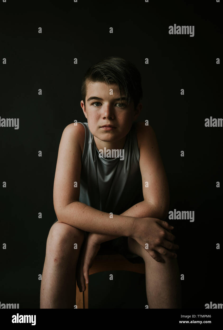 Portrait of confident serious boy sitting on stool against black ...