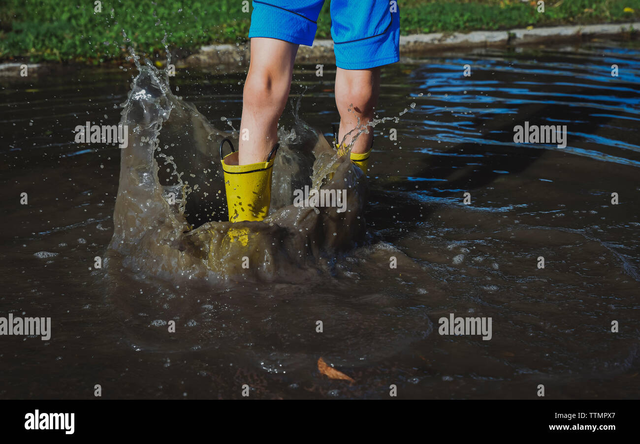 Low section of playful boy stamping Foot while standing in puddle at ...