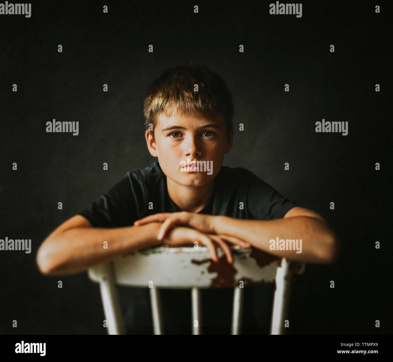 Portrait of confident boy sitting on chair against black background ...