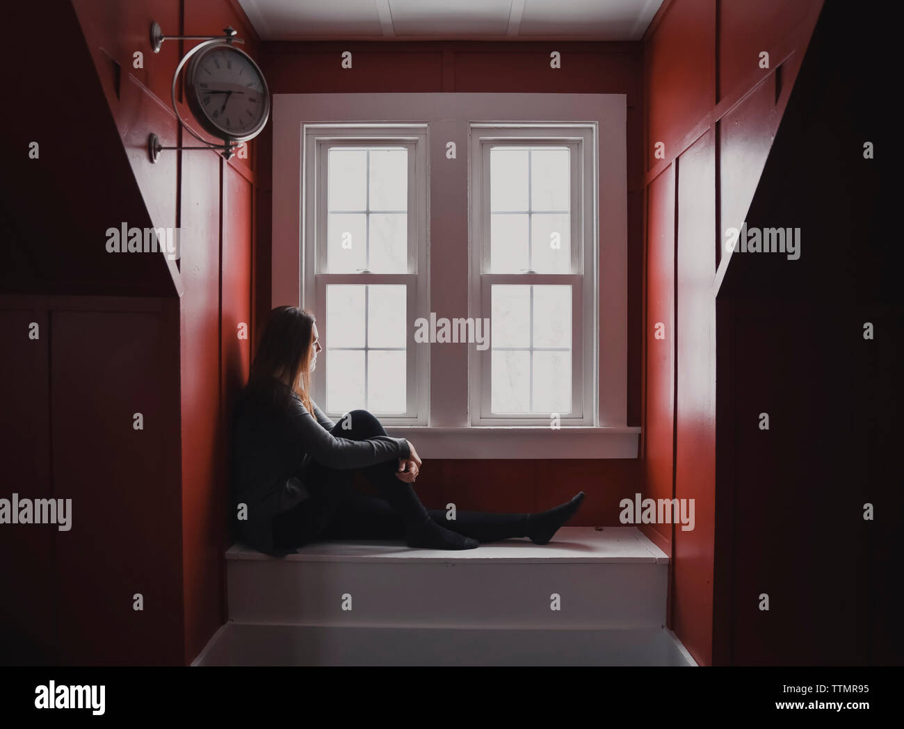 Woman sitting in window alcove looking out the window Stock Photo - Alamy