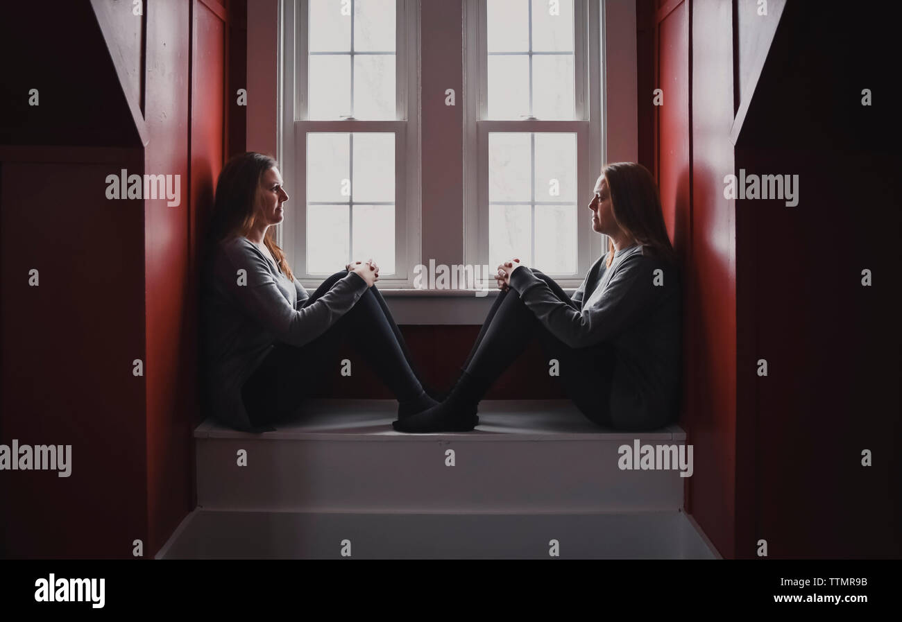 Twin women sitting in window alcove facing eachother Stock Photo - Alamy