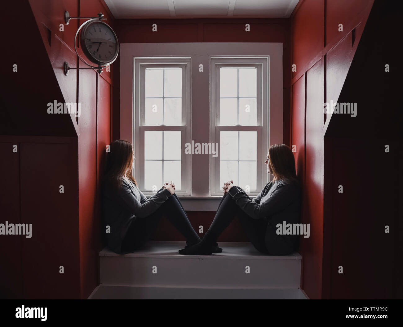 Twin women sitting in window alcove together looking out window Stock ...