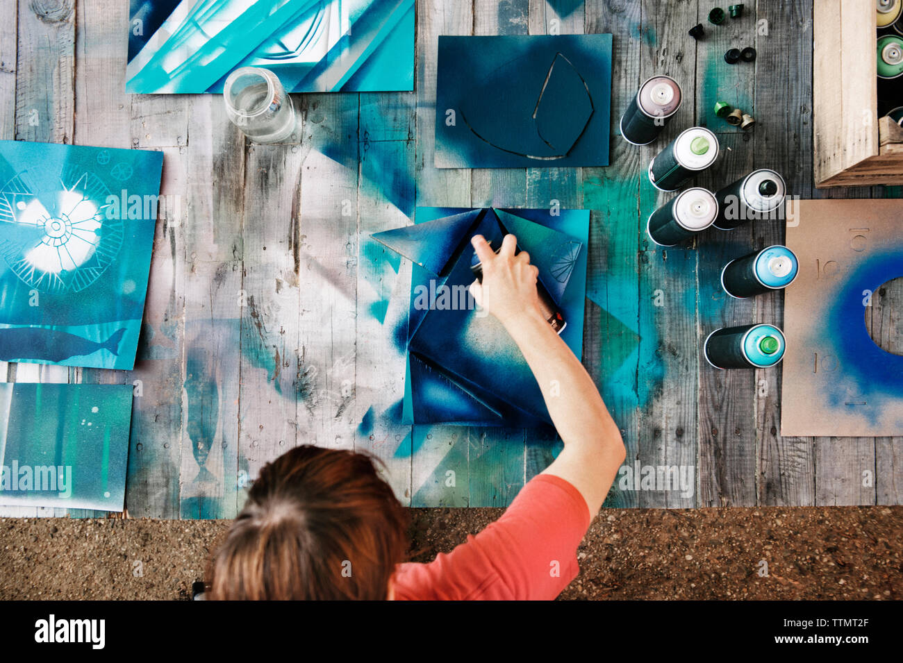 Overhead view of artist spraying paint on cardboard at table Stock ...