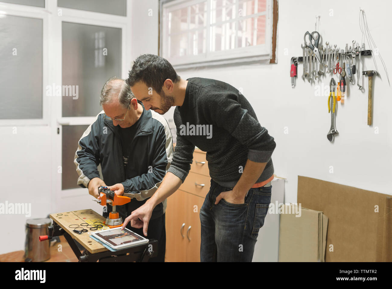 Mechanics watching tablet computer while using equipment at workshop ...
