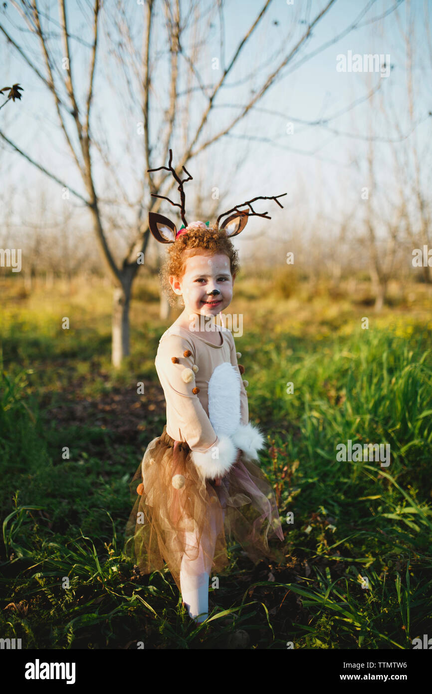 Portrait of cute girl in deer costume standing on grassy field against ...
