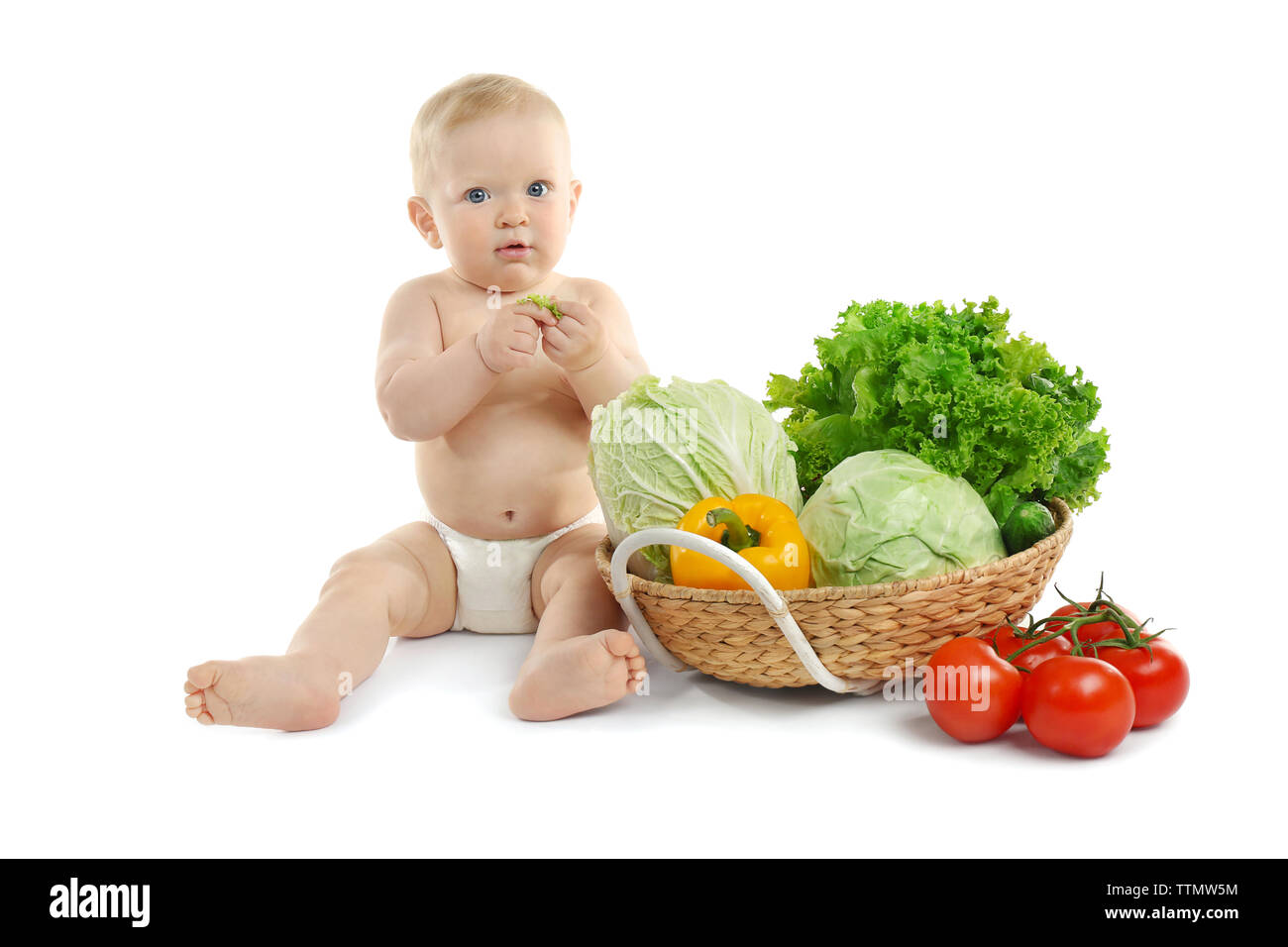 Cute baby and fresh vegetables in wicker basket on white background ...