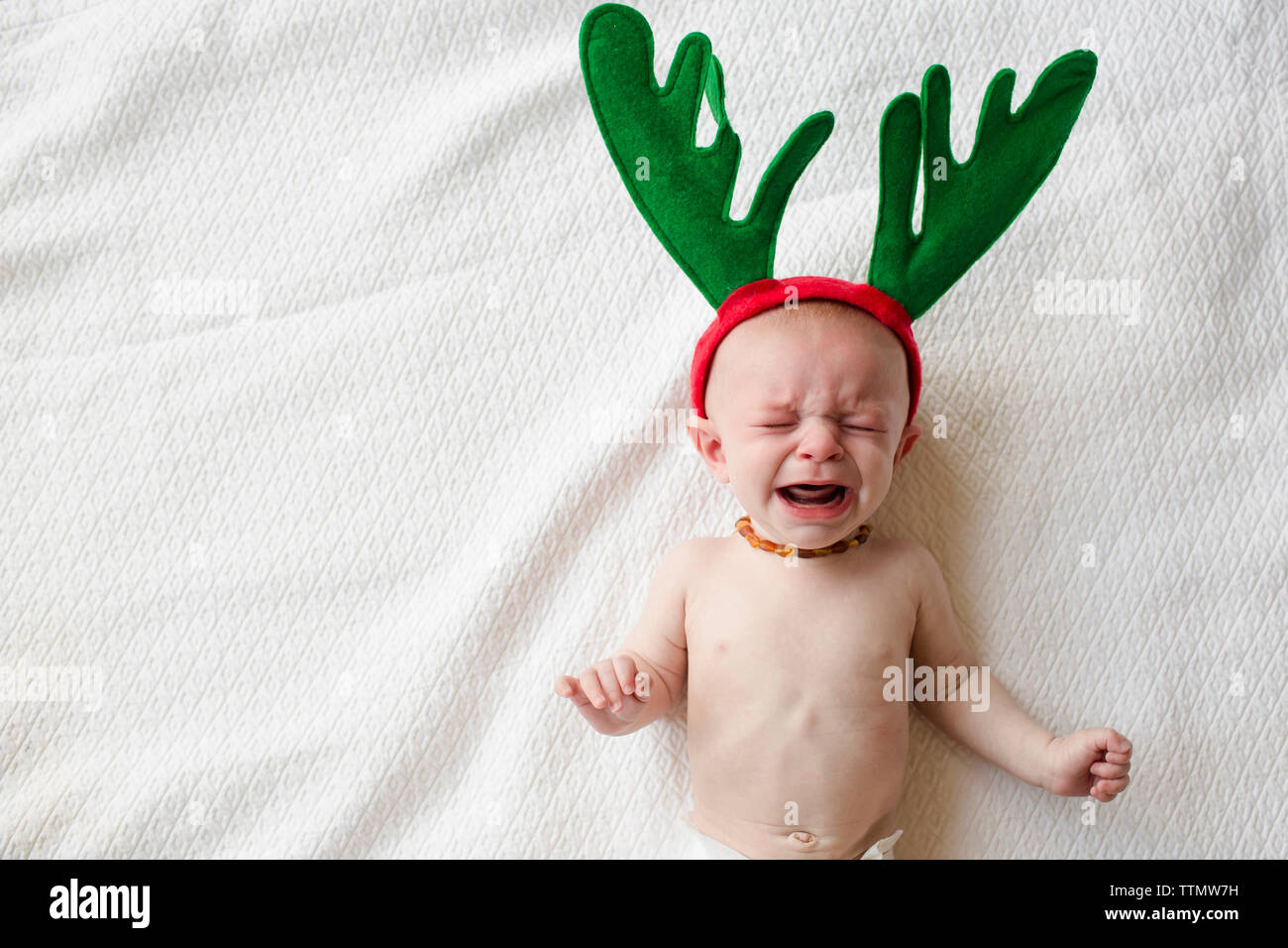 High angle view of cute baby boy in reindeer horns crying while lying ...