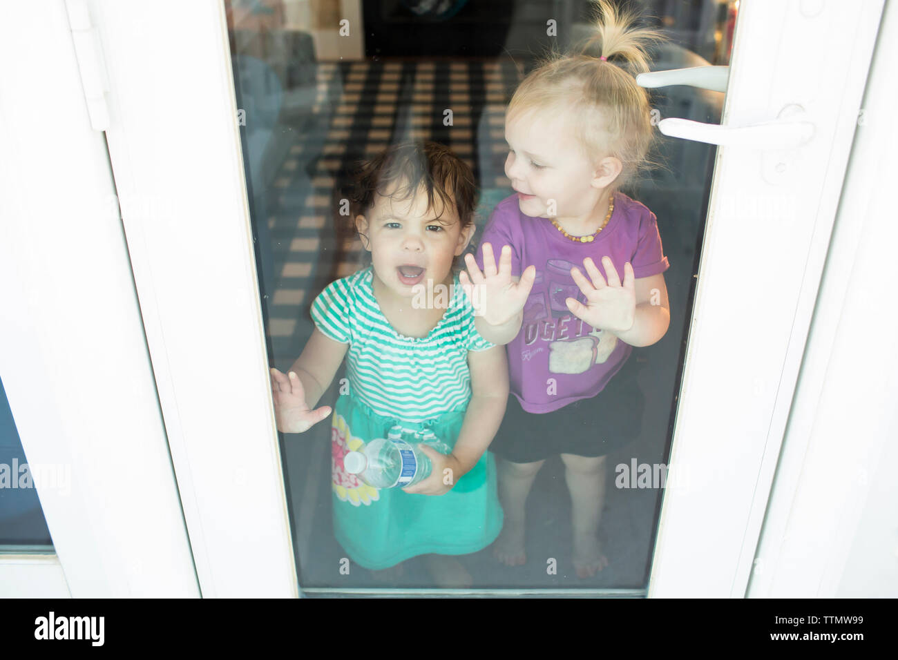 Sisters standing by door seen through glass Stock Photo - Alamy
