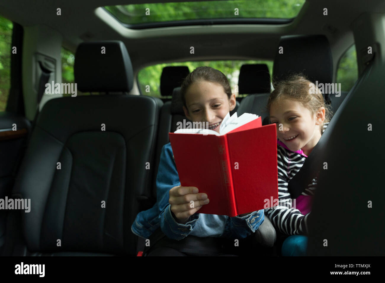 Happy sisters reading book while sitting in car Stock Photo - Alamy