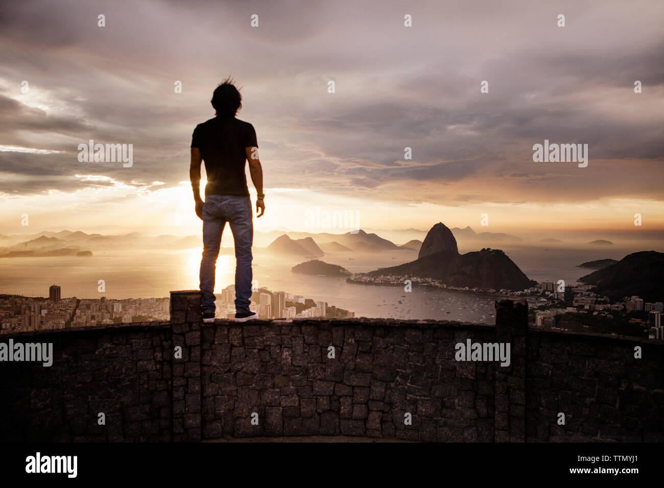 Rear view of silhouette man standing on retaining wall at observation ...