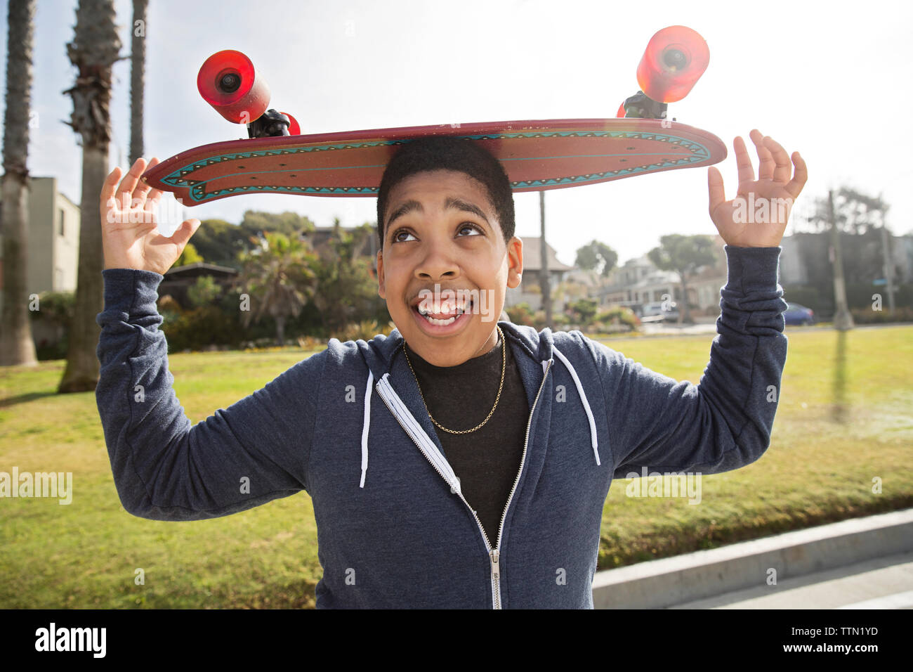 Playful teenage boy balancing skateboard on head at park Stock Photo ...