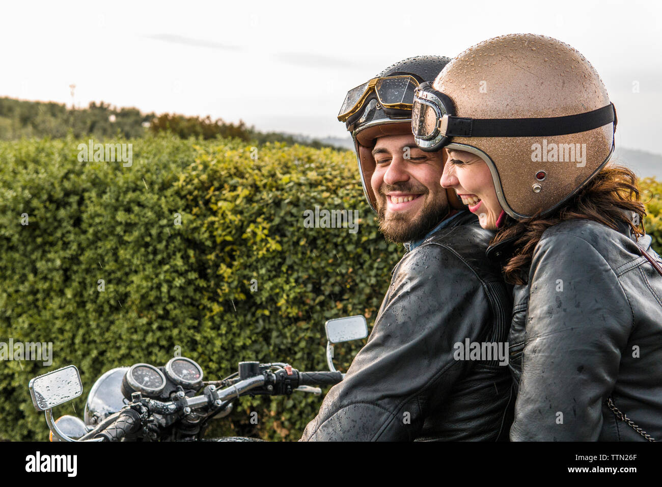 Cheerful couple talking while sitting on motorcycle against sky Stock ...