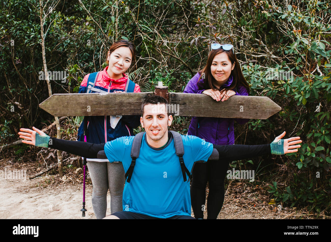 Portrait of happy friends standing by arrow symbol in forest Stock ...