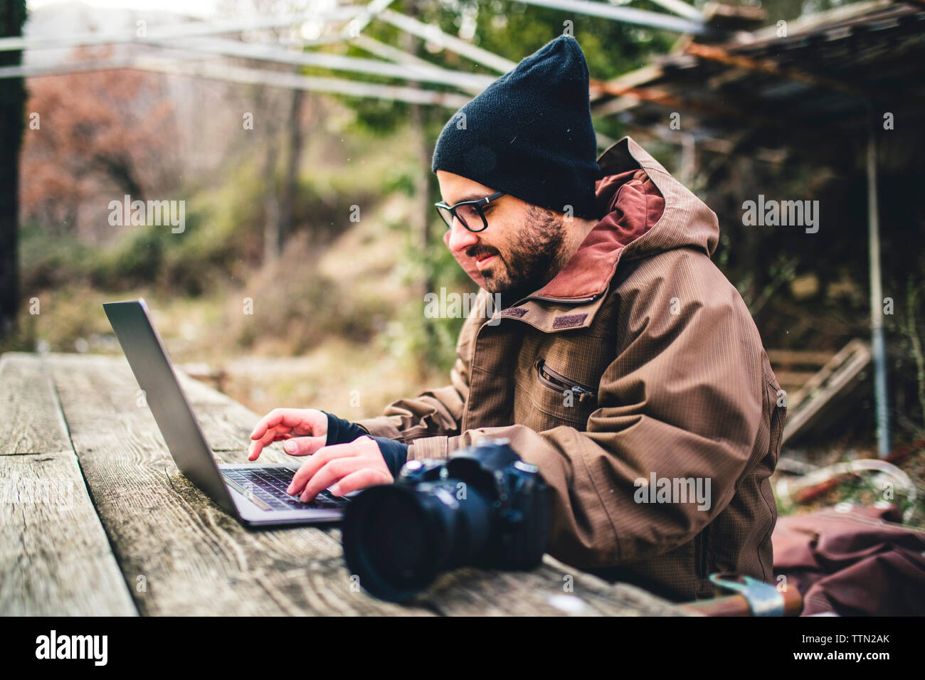 Side view of male hiker using laptop computer by camera on table in ...