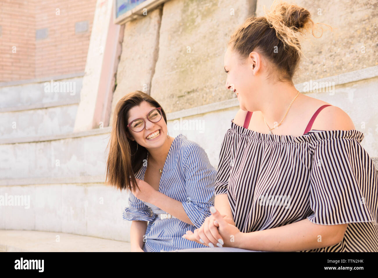 Happy female friends talking while sitting on steps Stock Photo - Alamy