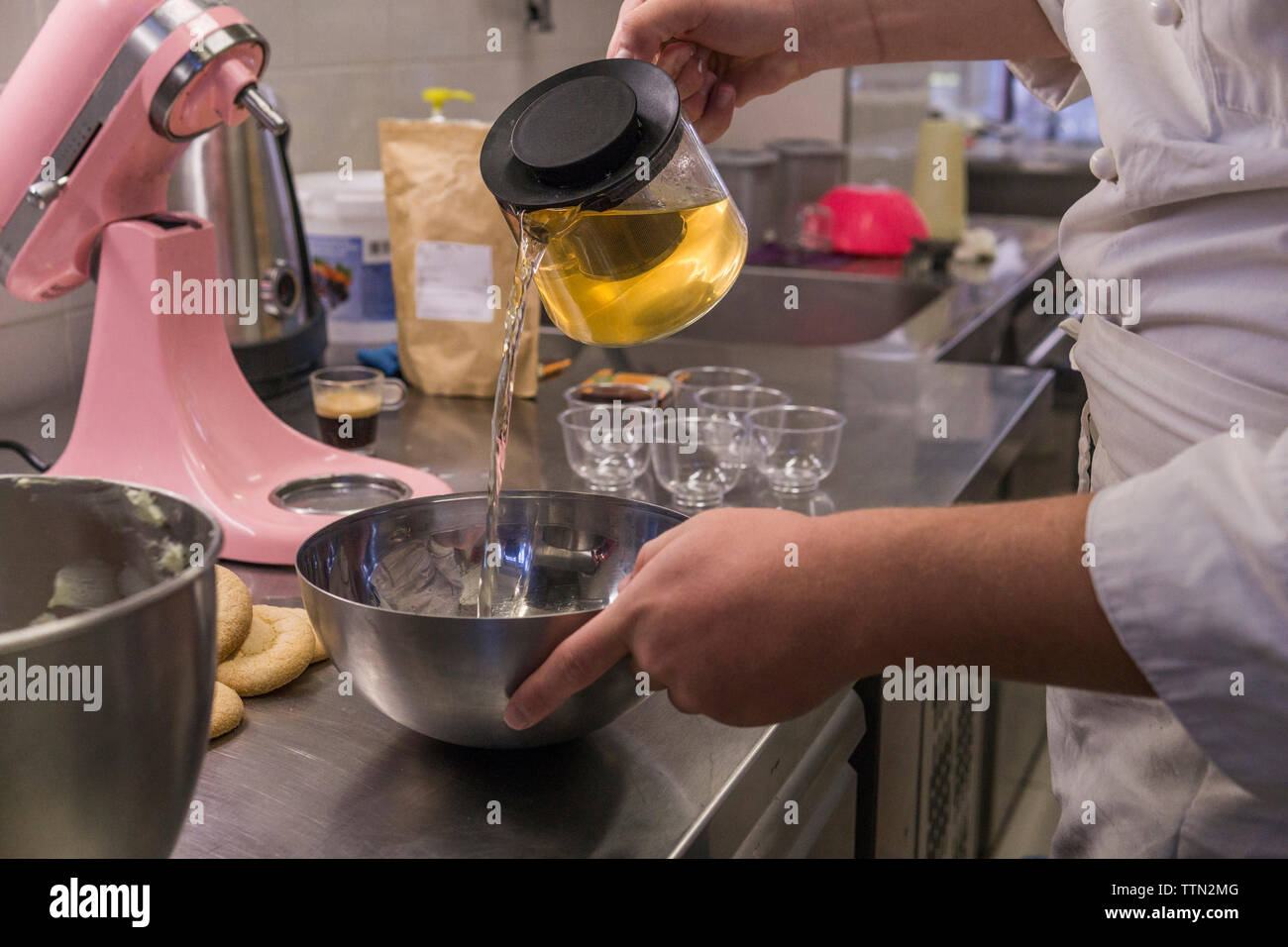 Midsection of male baker pouring water in mixing bowl on kitchen ...
