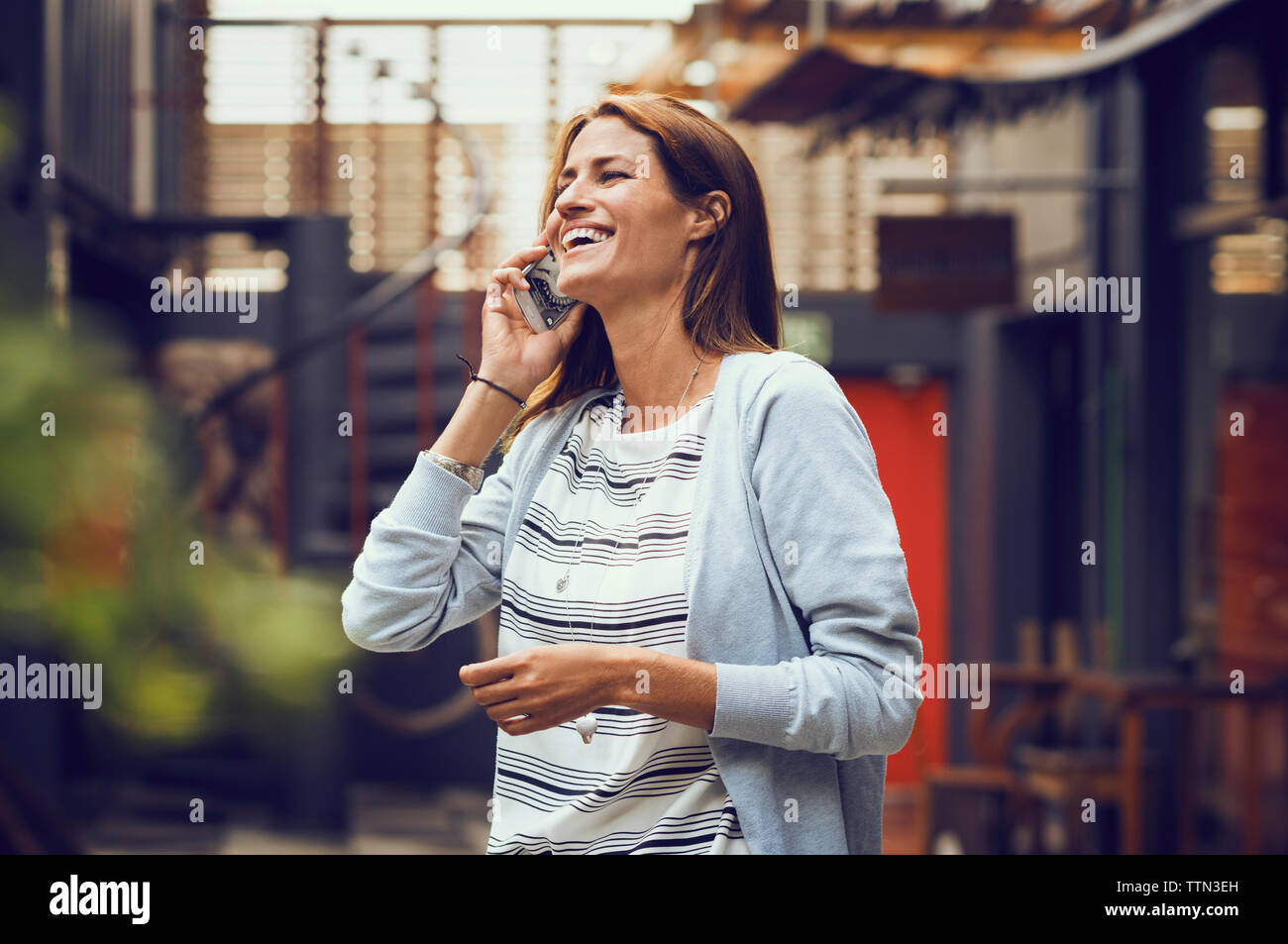 Cheerful woman answering smart phone outside cafe Stock Photo - Alamy