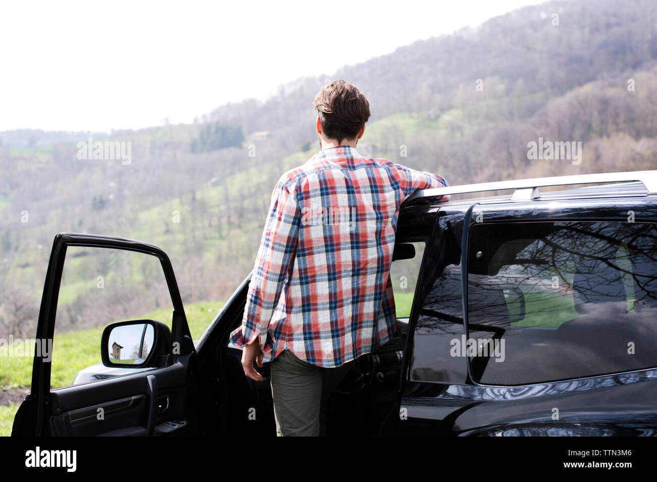 Rear view of man standing outside car on mountain Stock Photo - Alamy