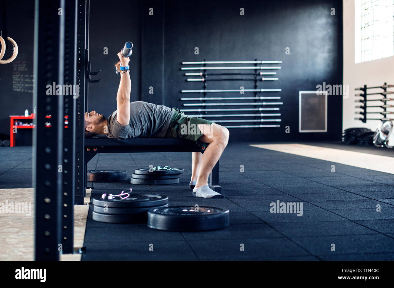 Side view of man lifting weight bar while lying on table in gym Stock ...