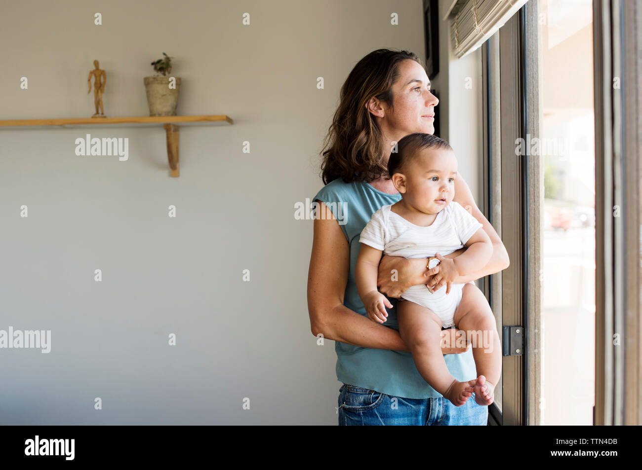 Mother with baby boy standing by window at home Stock Photo - Alamy