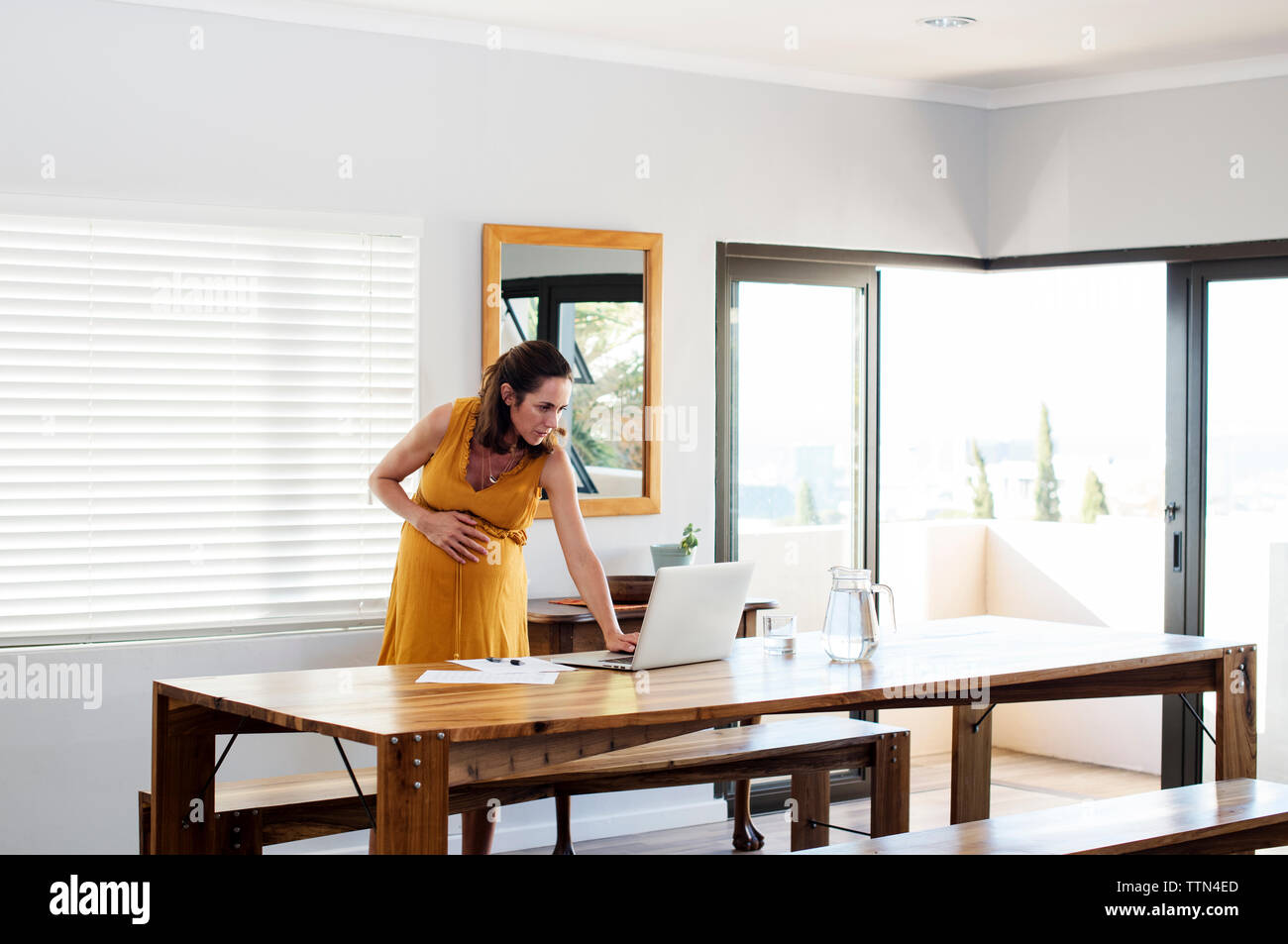 Pregnant woman using laptop computer while standing by table at home ...