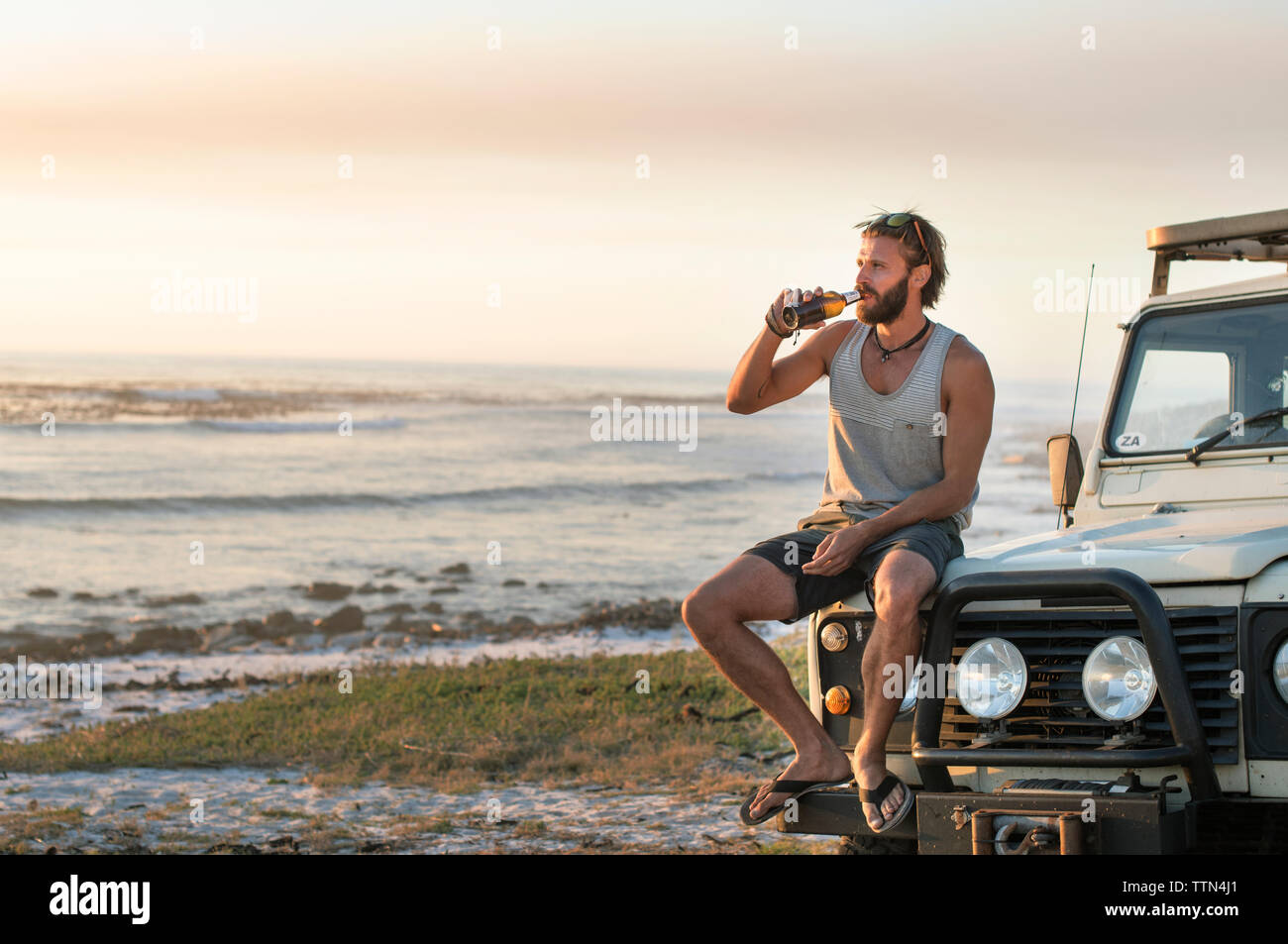 Man drinking beer while sitting on off-road vehicle at beach during ...