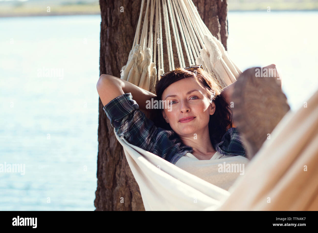 Portrait of woman relaxing on hammock by tree at lakeshore Stock Photo ...