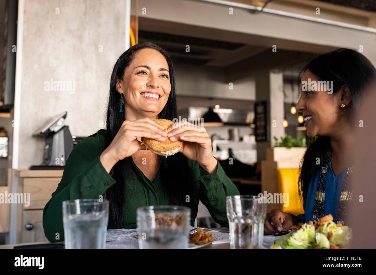 Happy female friends talking while eating food in cafeteria Stock Photo ...