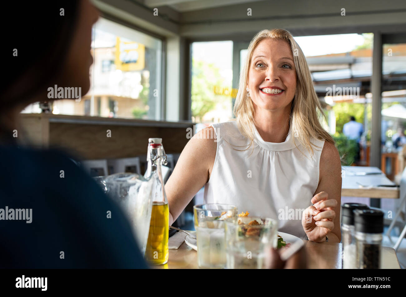 Happy female friends talking while eating food on table in cafeteria ...