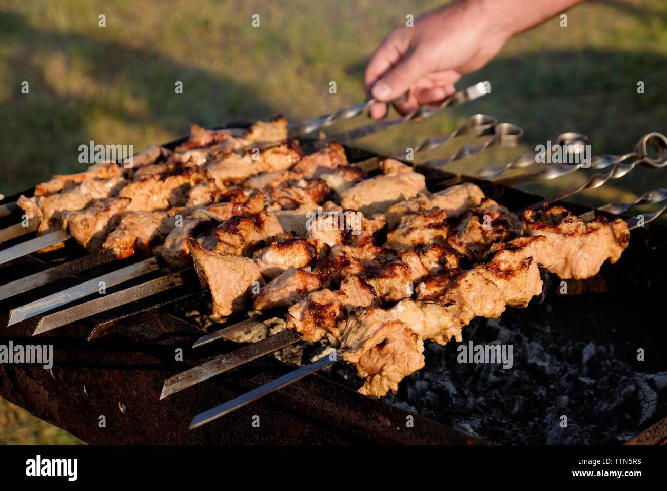 Male hand rotating meat pieces on skewer roasting in brazier Stock ...