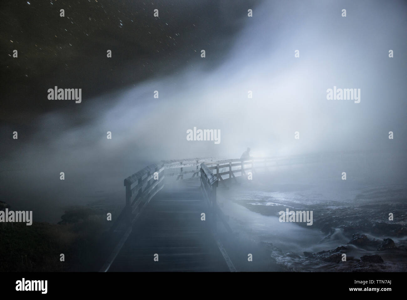 Man standing on footbridge over geyser amidst steam at Yellowstone ...