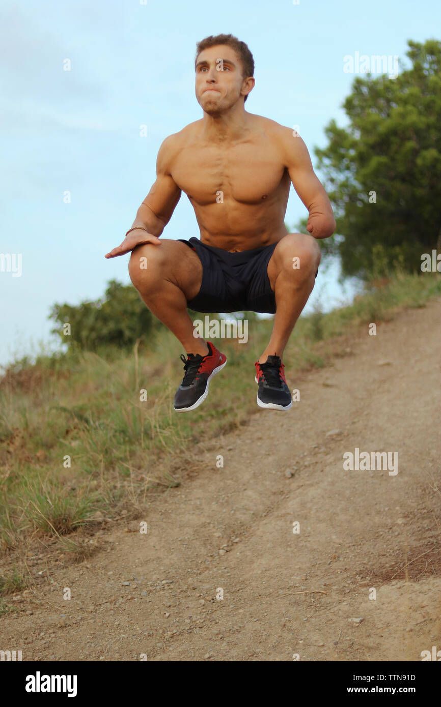 Physically challenged shirtless man jumping while exercising on field ...