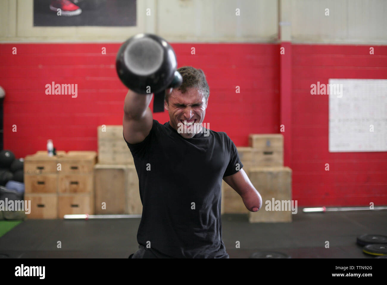 Male adaptive athlete lifting kettlebell while standing against wall in ...