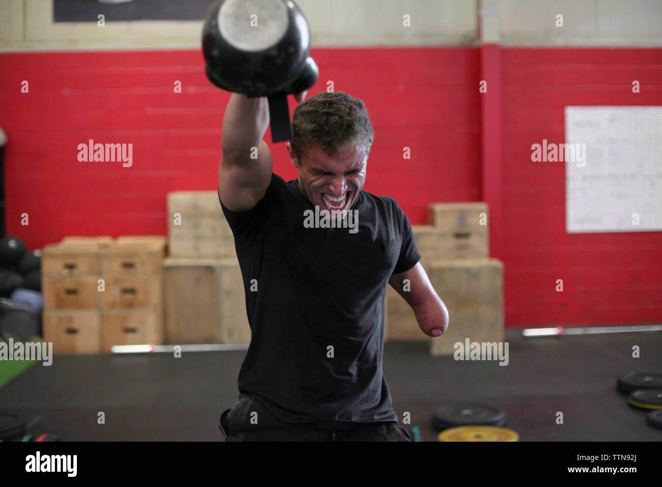 Aggressive male adaptive athlete lifting kettlebell while standing ...
