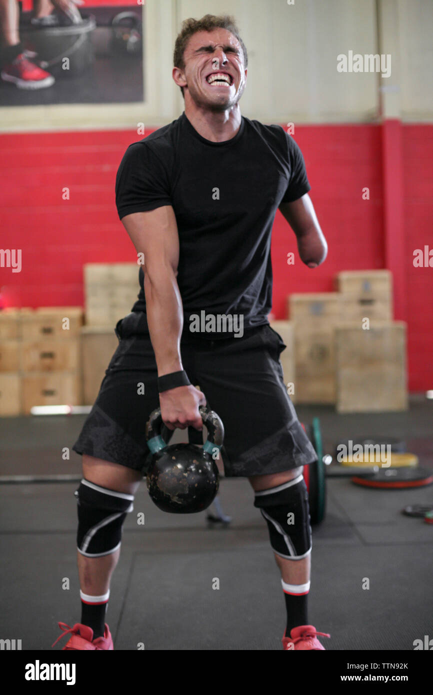 Full length of aggressive male adaptive athlete lifting kettlebell ...