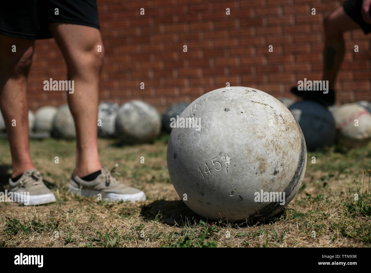 Low section of male athletes with atlas stones standing on grassy field ...