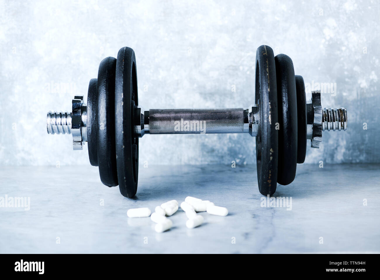 Black heavy dumbbell and creatine capsules on rustic background ...