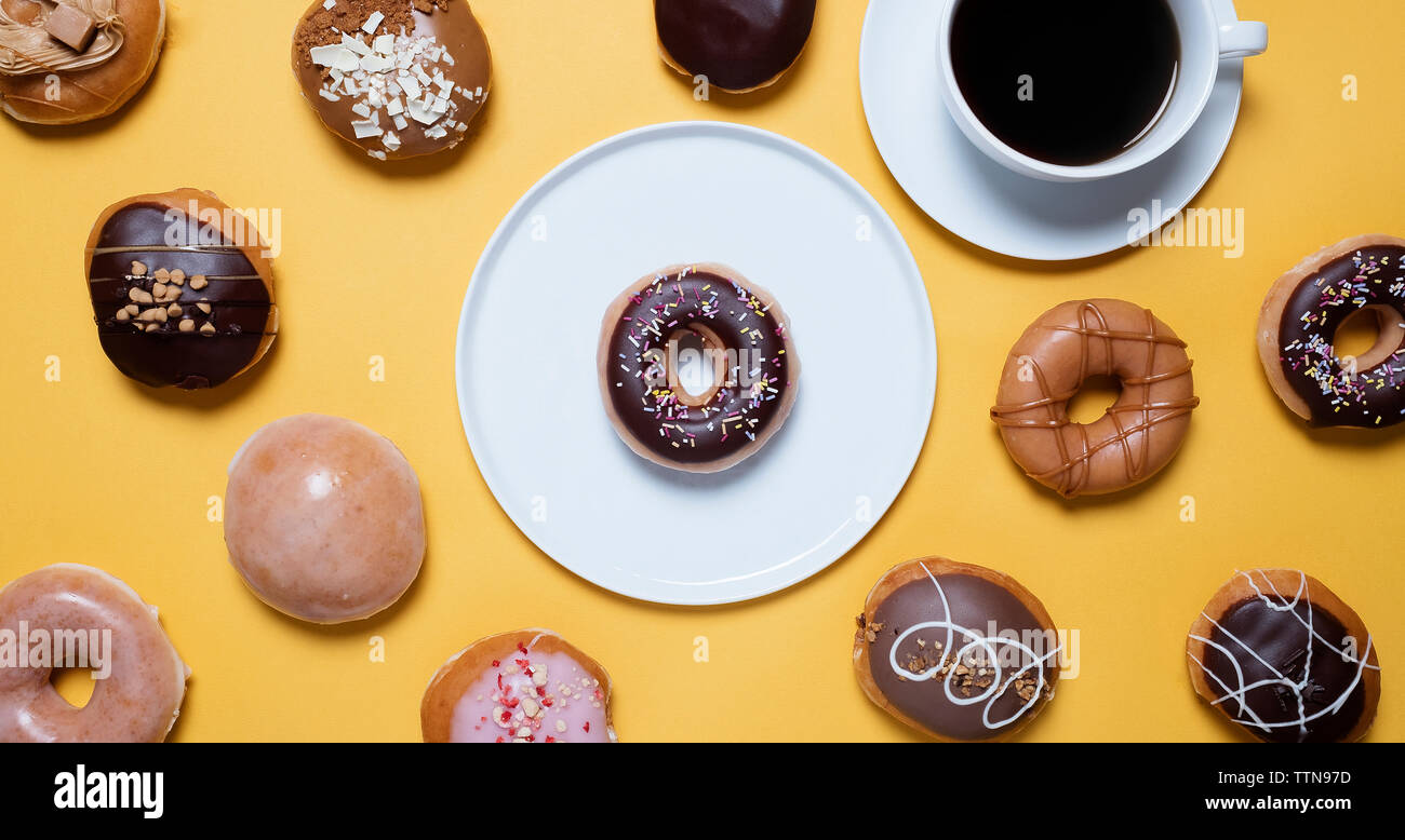 Overhead view of various donuts with coffee arranged on yellow ...