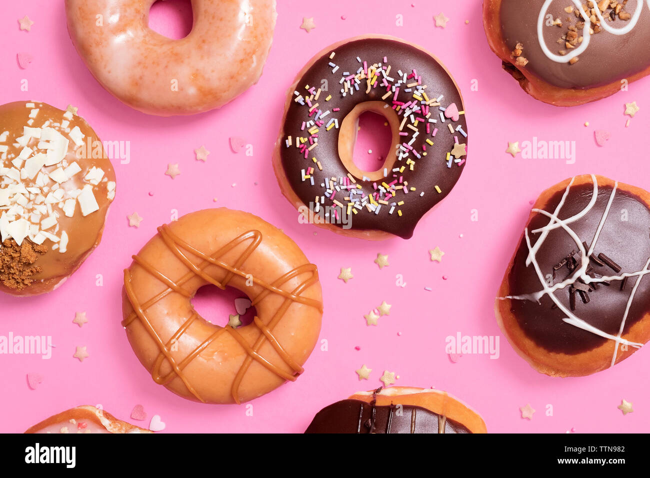Overhead view of various donuts with confetti arranged on pink ...