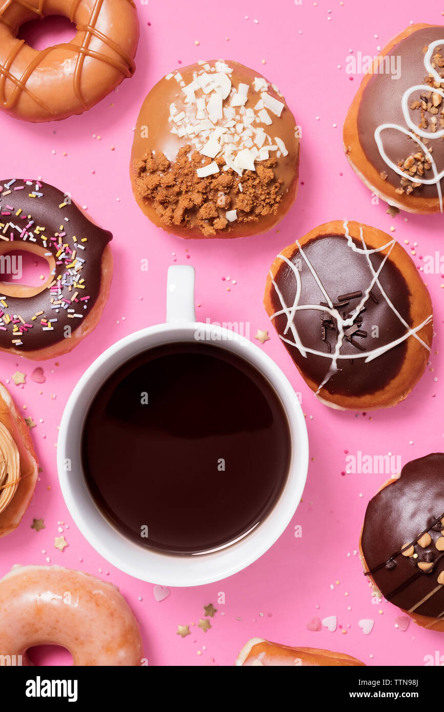 Overhead view of various donuts with coffee arranged on pink background ...