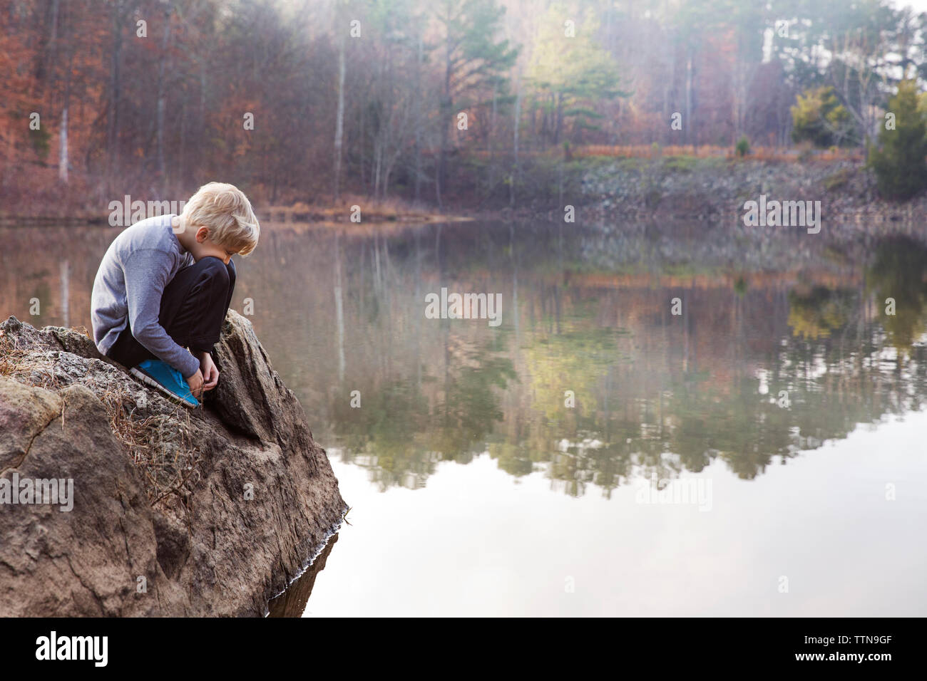 Boy sitting on rock by lake Stock Photo - Alamy