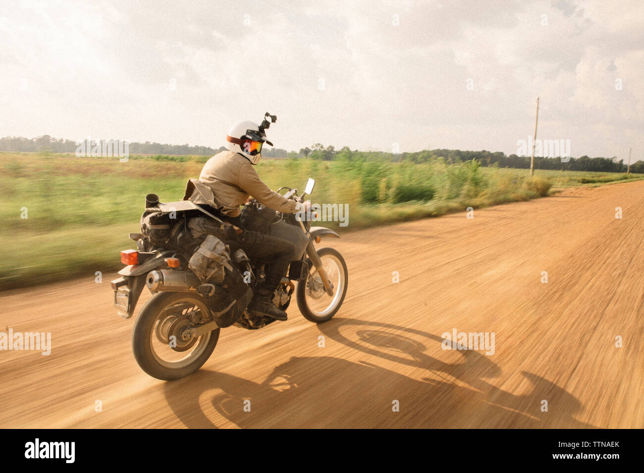 Biker wearing crash helmet while riding motorcycle on dirt road against ...
