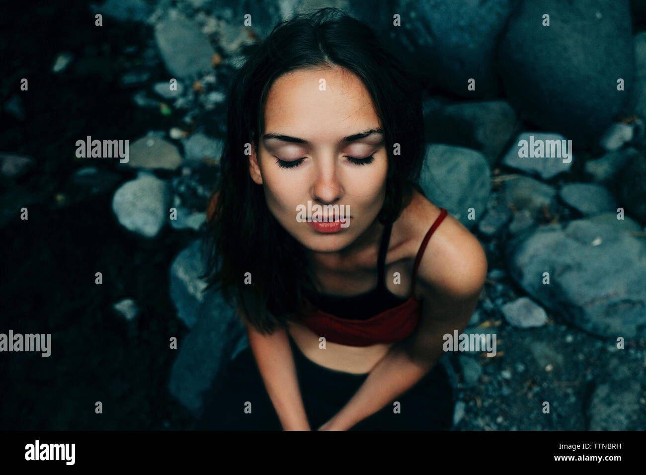 High angle view of woman with eyes closed sitting on rocks in forest ...